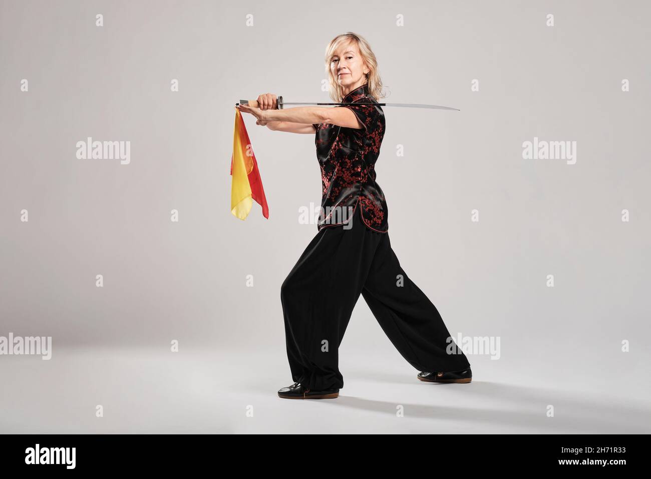 Mature blonde woman practicing Tai Chin with saber in a white ...
