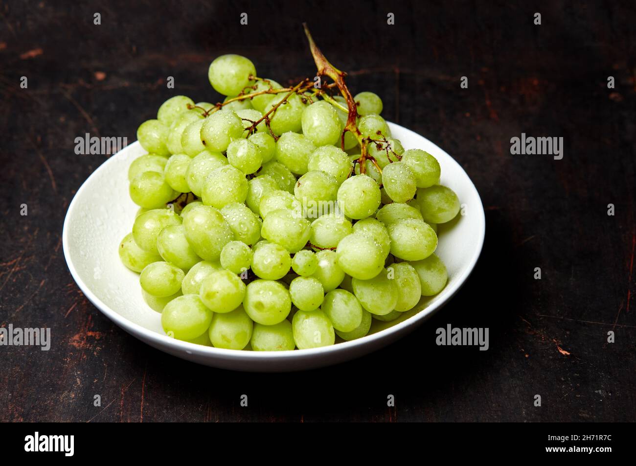 Branch of ripe green grape on plate with water drops. Juicy grapes on wooden background, closeup ...