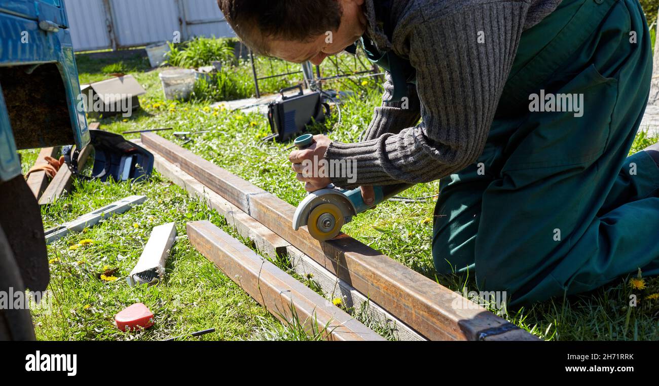 Man grinds a metal product with angle grinder outdoors. Metal ...