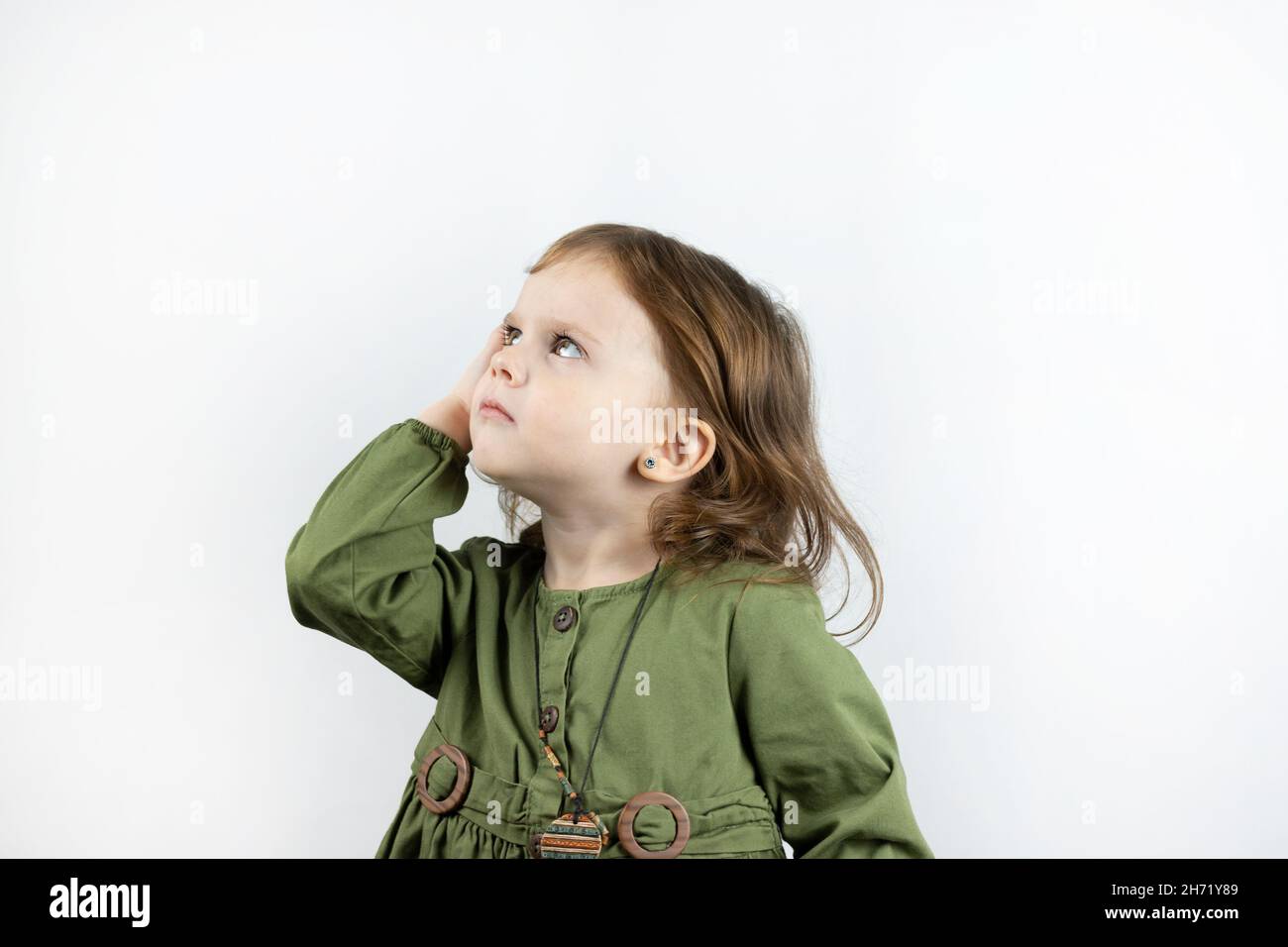 A small child with red hair, thinking, looks up and puts his hand to ...