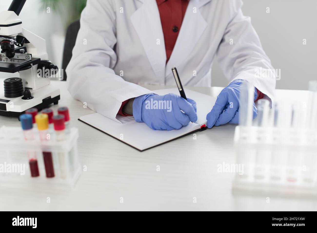 cropped view of scientist in latex gloves writing in notebook near test ...