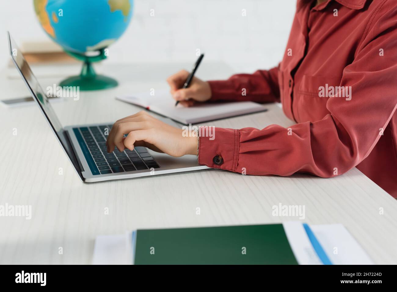 cropped view of young teacher using laptop and writing in notebook ...