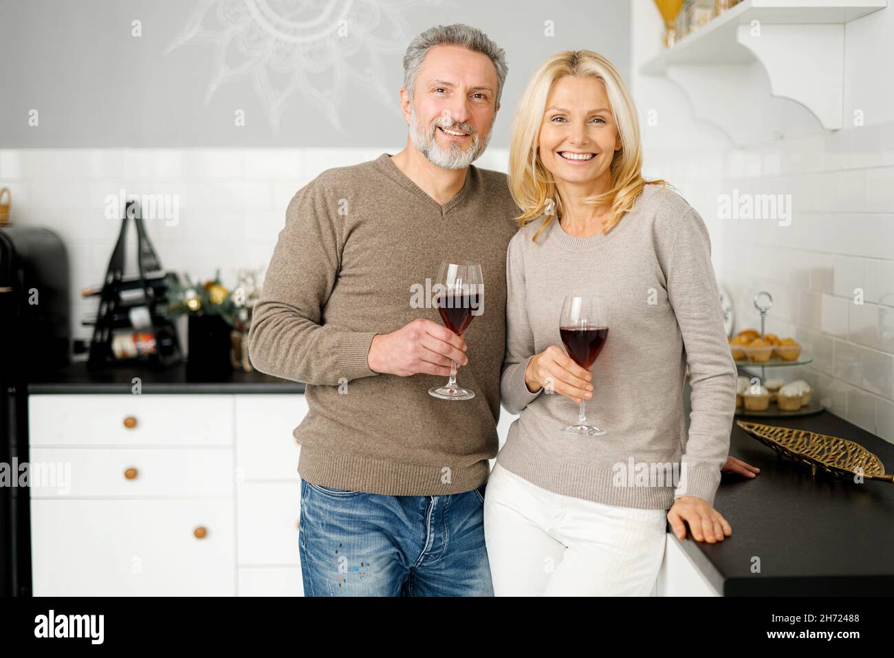 Middle-aged couple holding glasses of wine look at camera and smiles ...