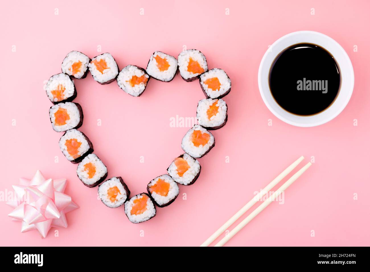 Salmon sushi rolls laid out in the shape of a heart on a pink ...