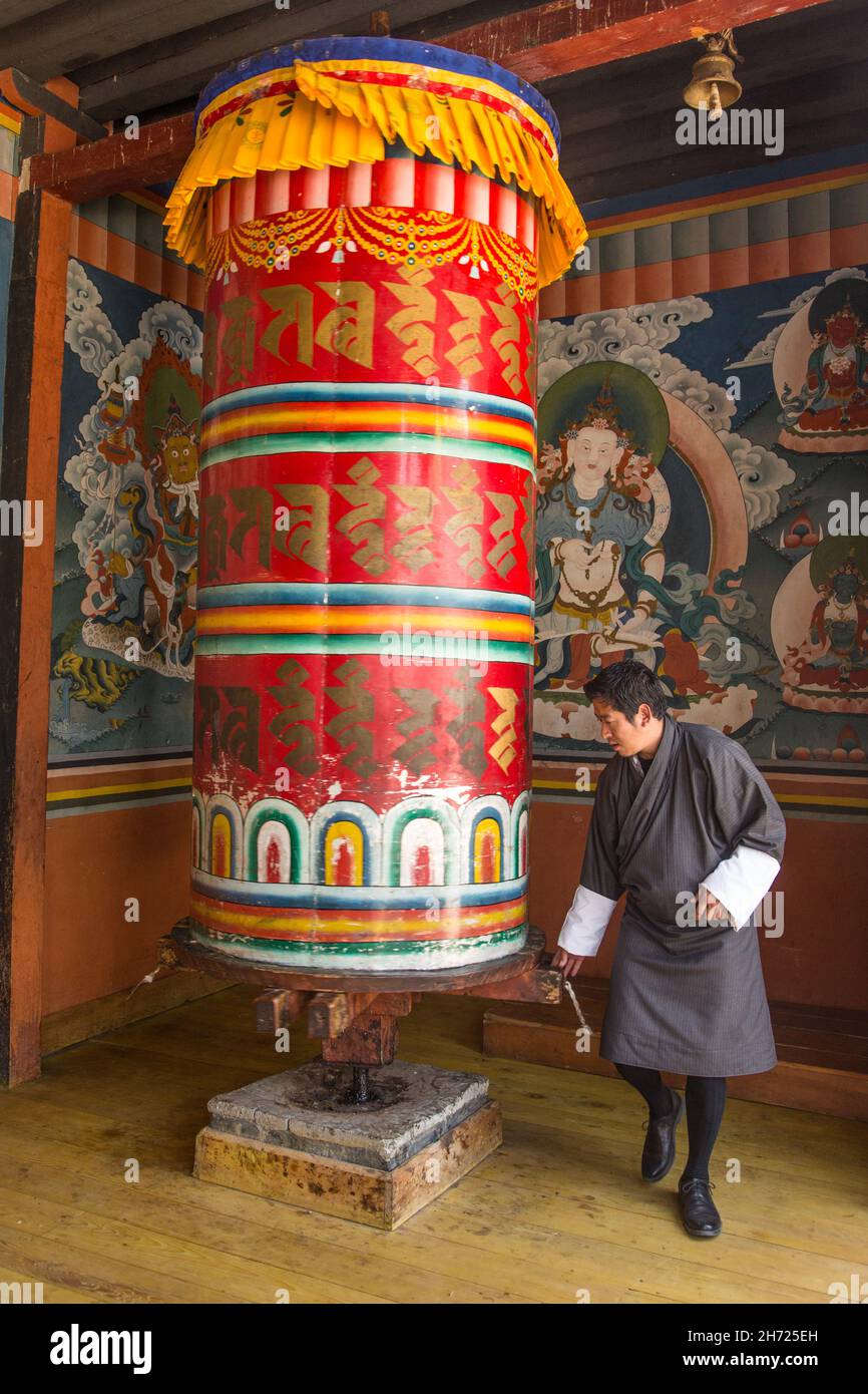 A Bhutanese man in the traditiona gho robe turns a large prayer wheel ...