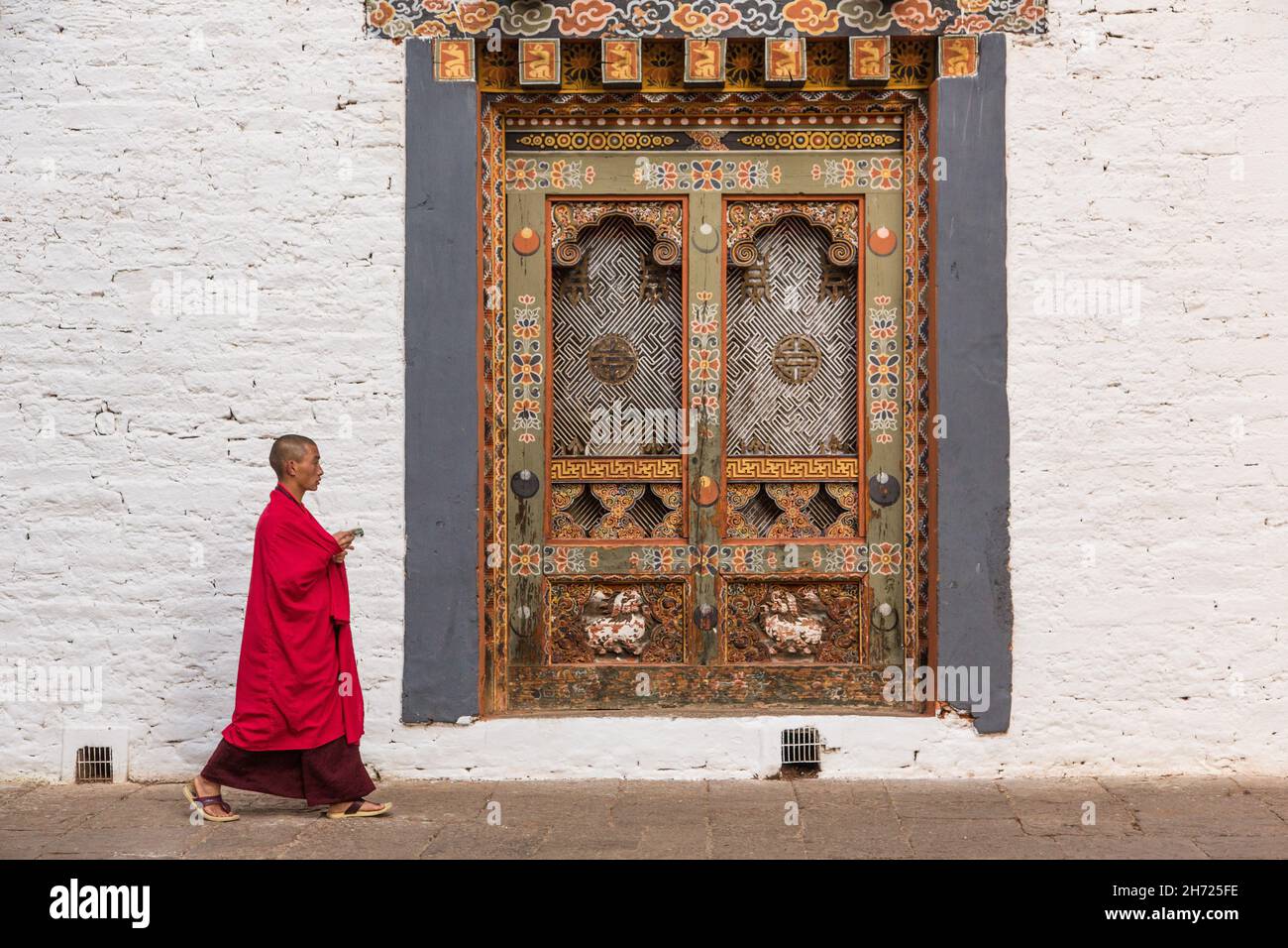 A Buddhist monk walks past a lattice-work window in a dochey or ...