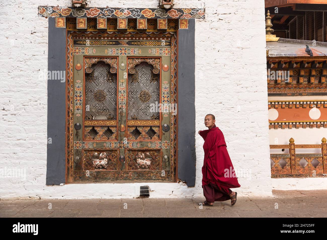 A Buddhist monk walks past a lattice-work window in a dochey or ...
