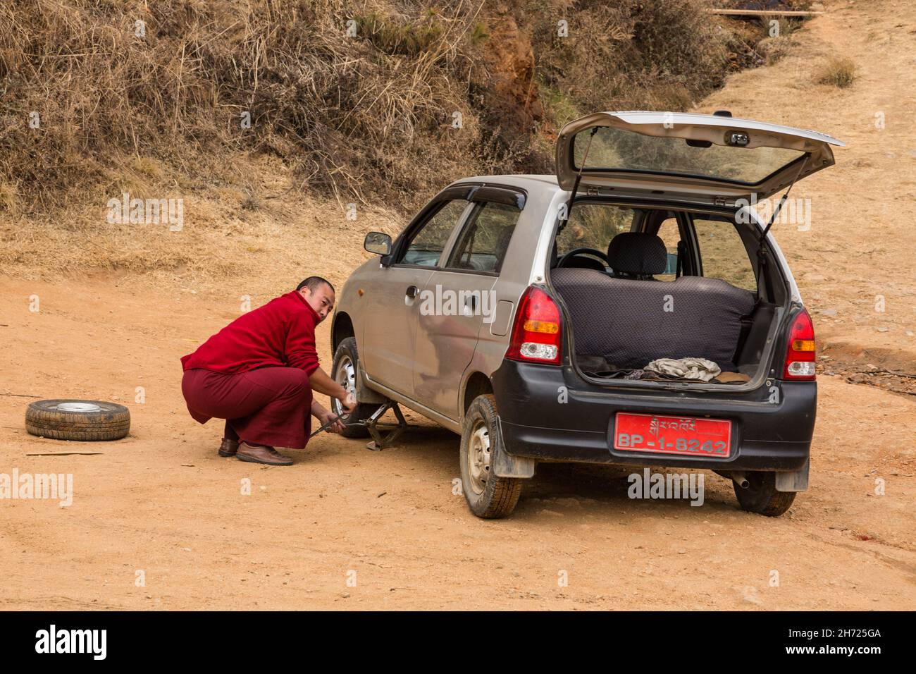 A Buddhist monk changes a tire on his car in Thimphu, Bhutan Stock ...