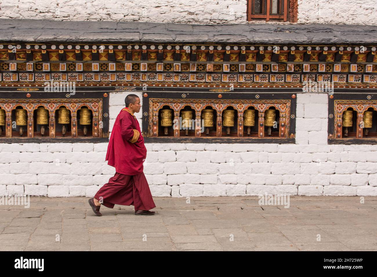 A Buddhist monk walks past a wall of prayer wheels in a dochey or ...