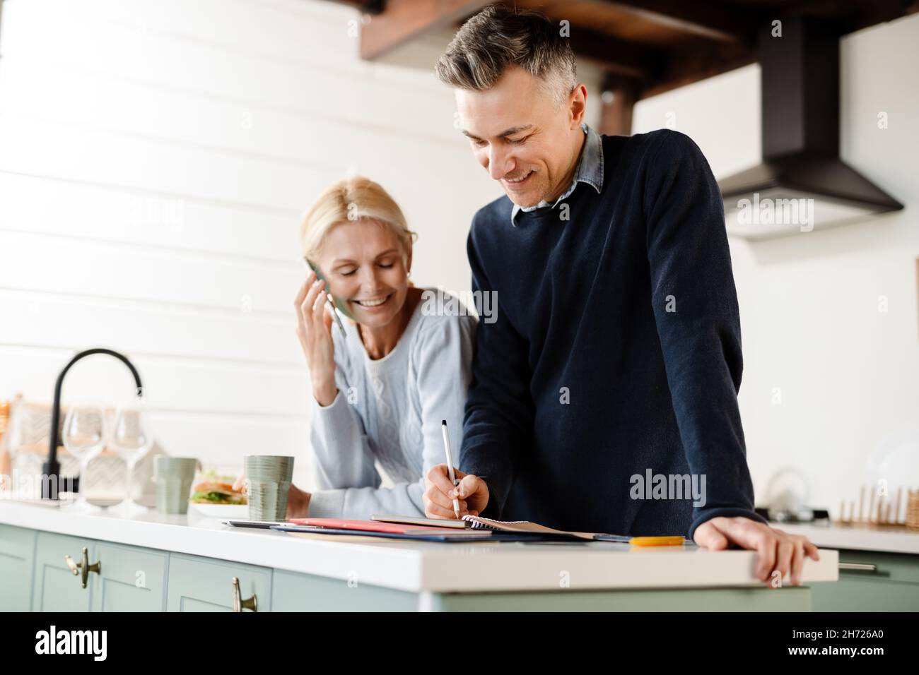 Smiling mid aged couple using cellphone and making notes in planner in ...