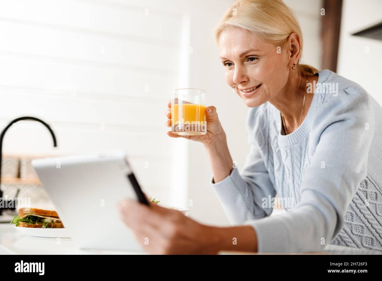 Smiling mid aged blonde woman holding tablet computer leaning on a ...