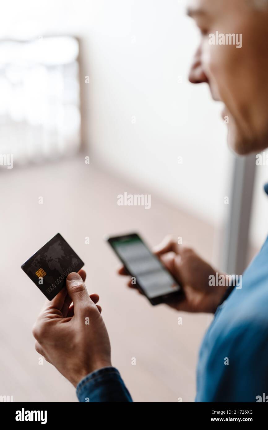 Mid aged casual man holding mobile phone amd credit card standing ...