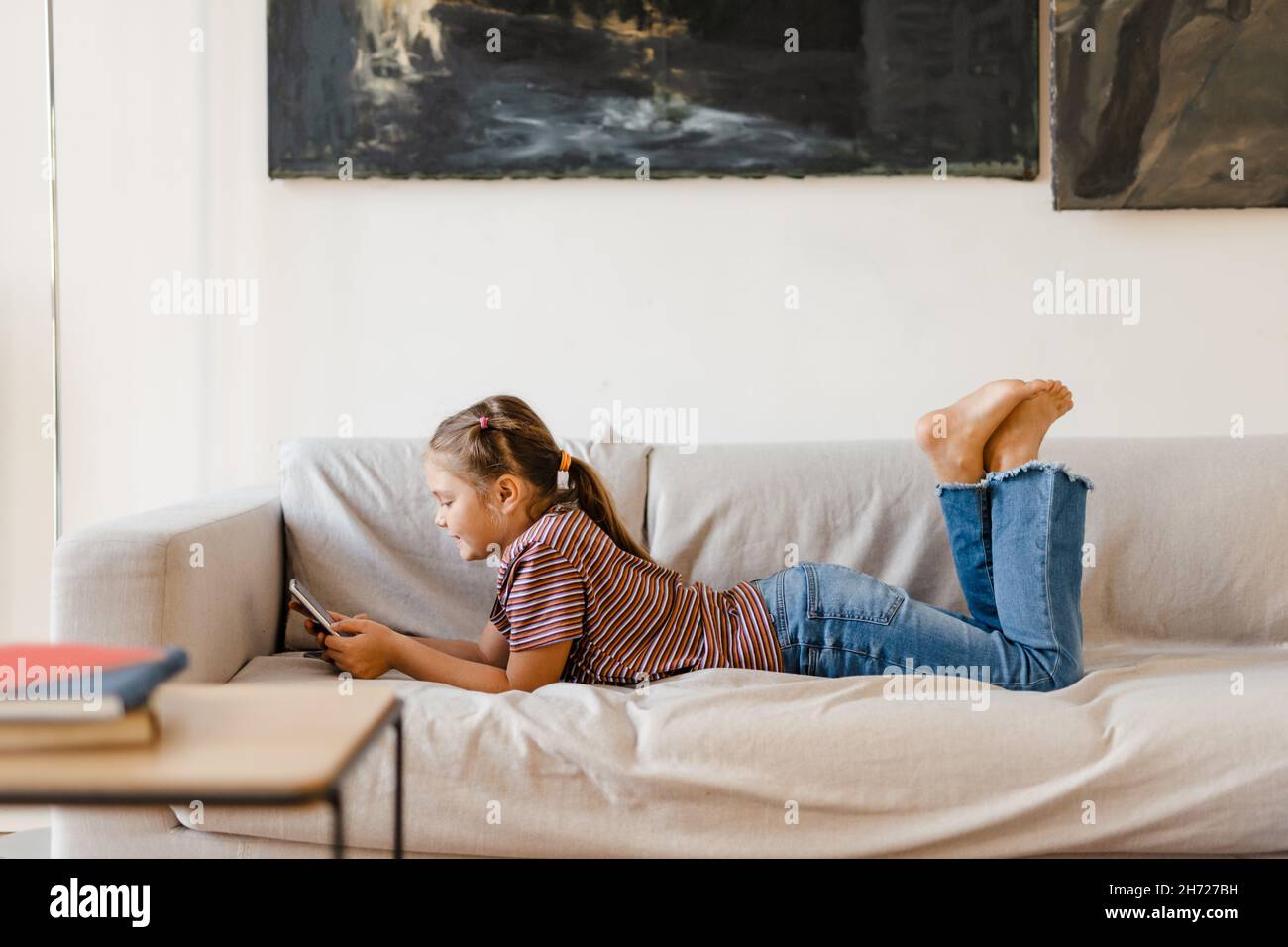 White preteen girl smiling and using mobile phone while lying on couch ...