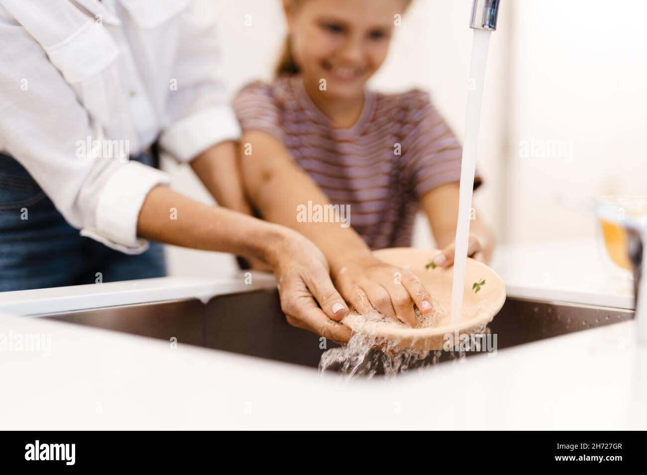 White mother and daughter smiling while washing dishes together in ...