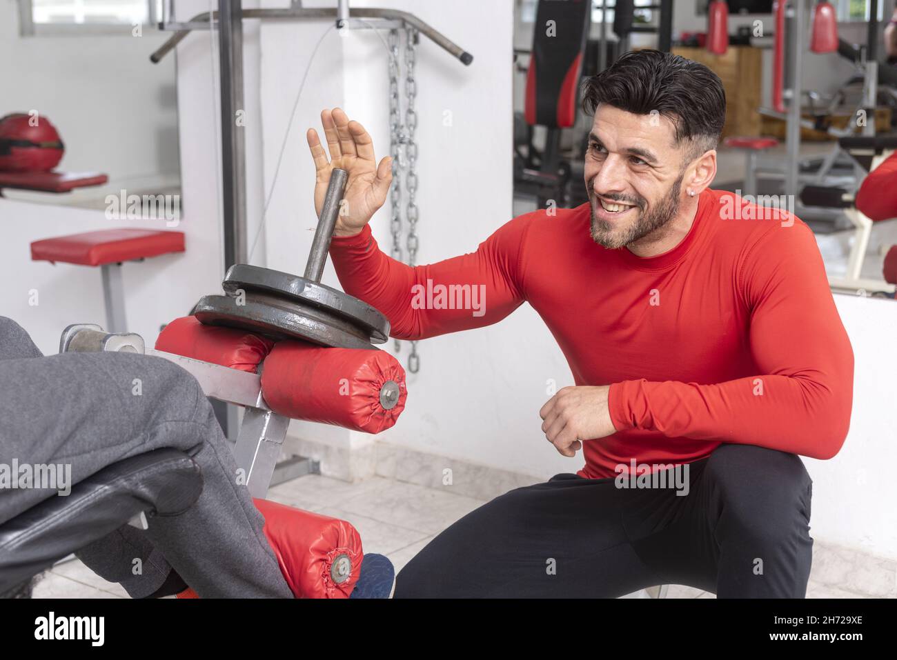 Young gym trainer helping to lift heave barbell with legs Stock Photo ...
