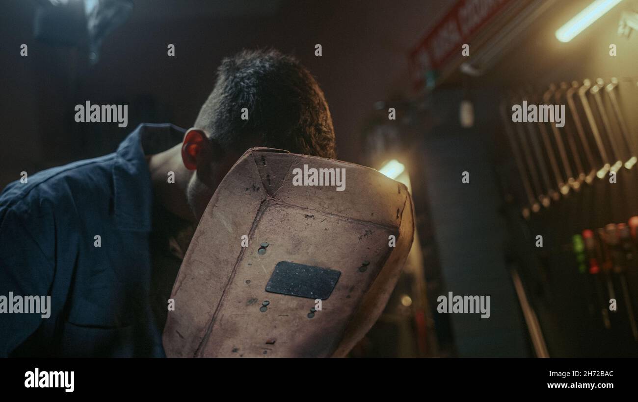 Young blacksmith man with welding shield using welding machine for ...