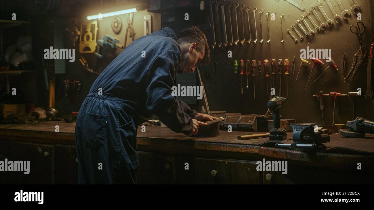 Blacksmith young man in awesome workshop background he sanding a piece ...