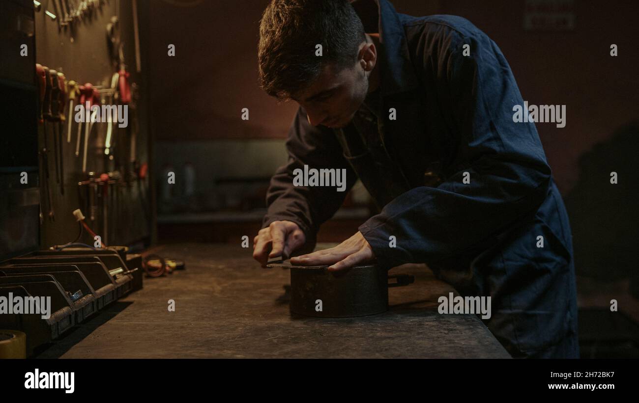 Young blacksmith man sanding a piece of iron or steel in his workshop ...