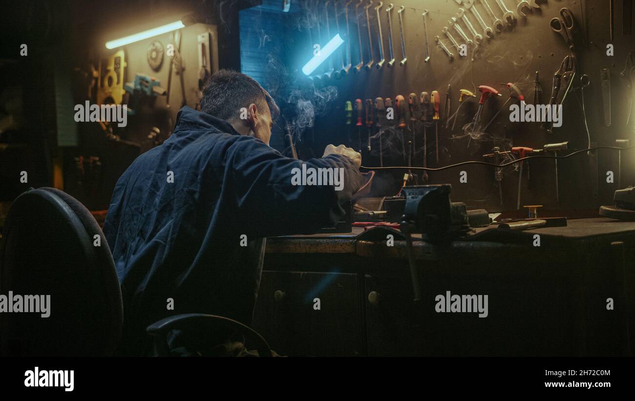 Young blacksmith man with workwear, taking solder tool, sitting on ...