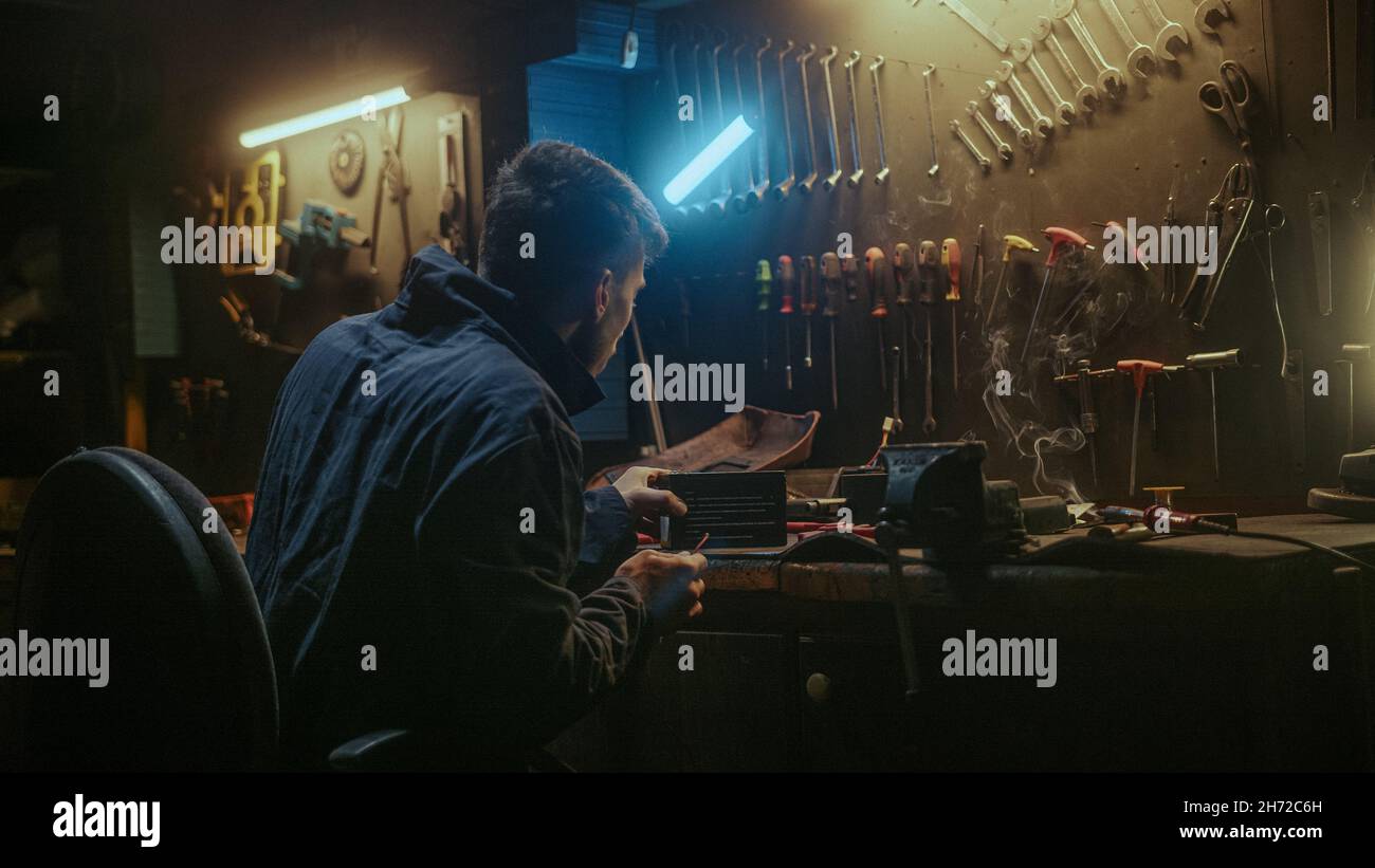 Young blacksmith man with workwear, taking solder tool, sitting on ...