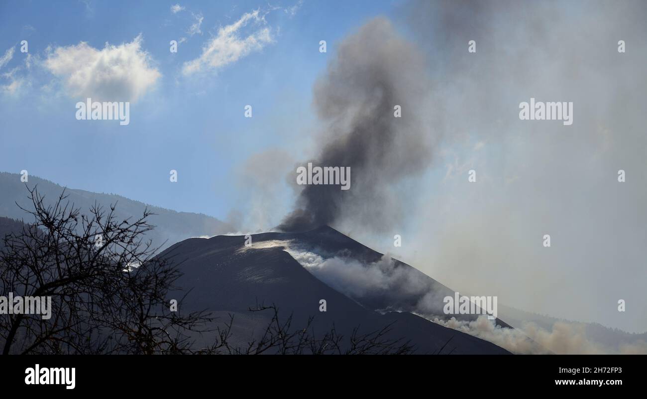 Volcano in full eruption, bushes in the foreground and blue sky in the ...
