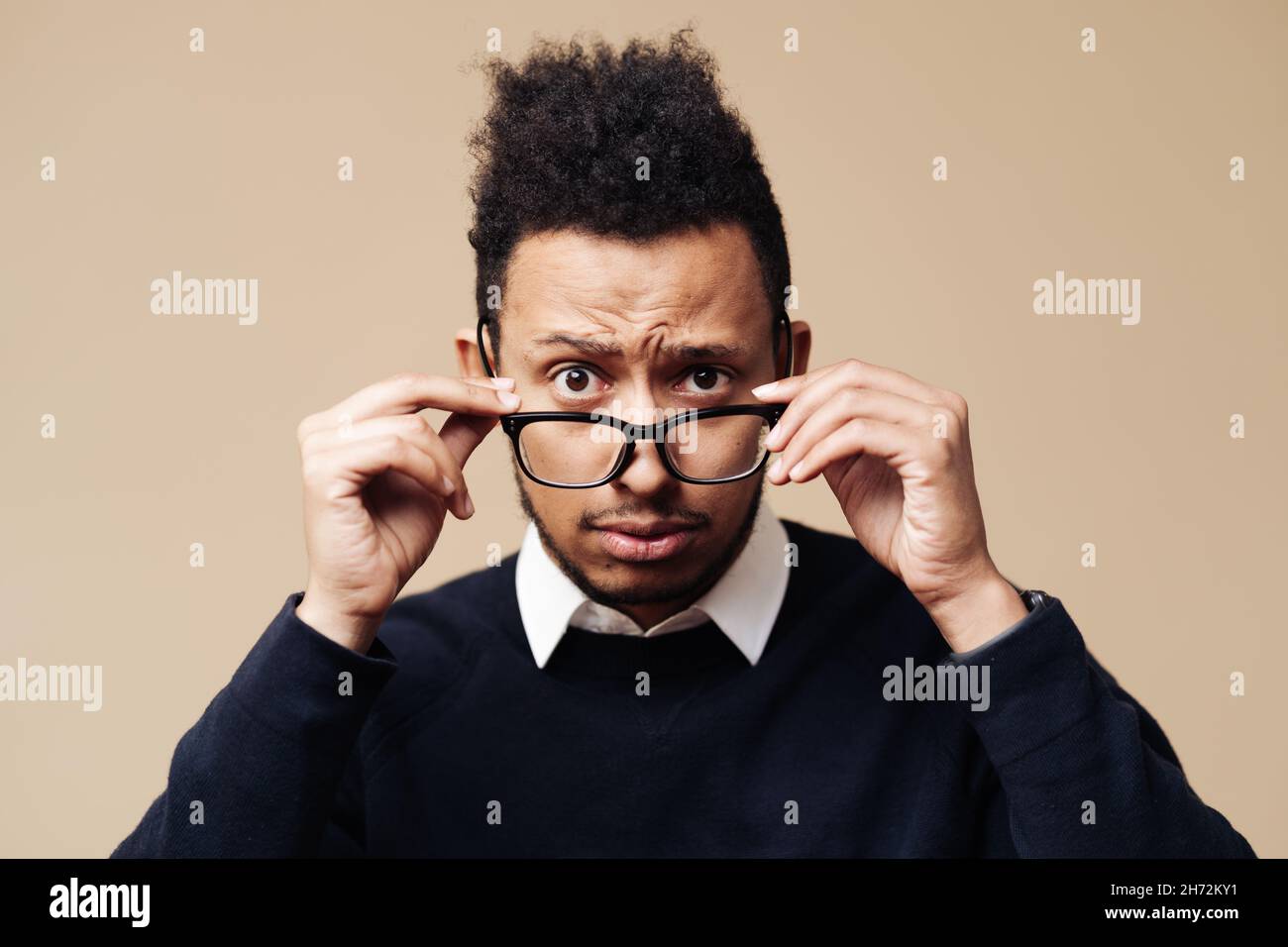Young worried Afro man looking over glasses on beige background. Face ...