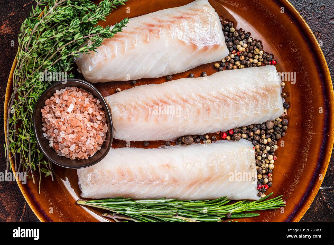 Raw Haddock loin fillet fish on rustic plate with thyme and salt. Dark ...