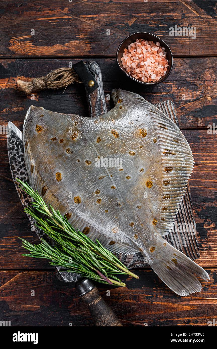 Raw plaice flatfish fish on butcher board with knife. Dark wooden ...