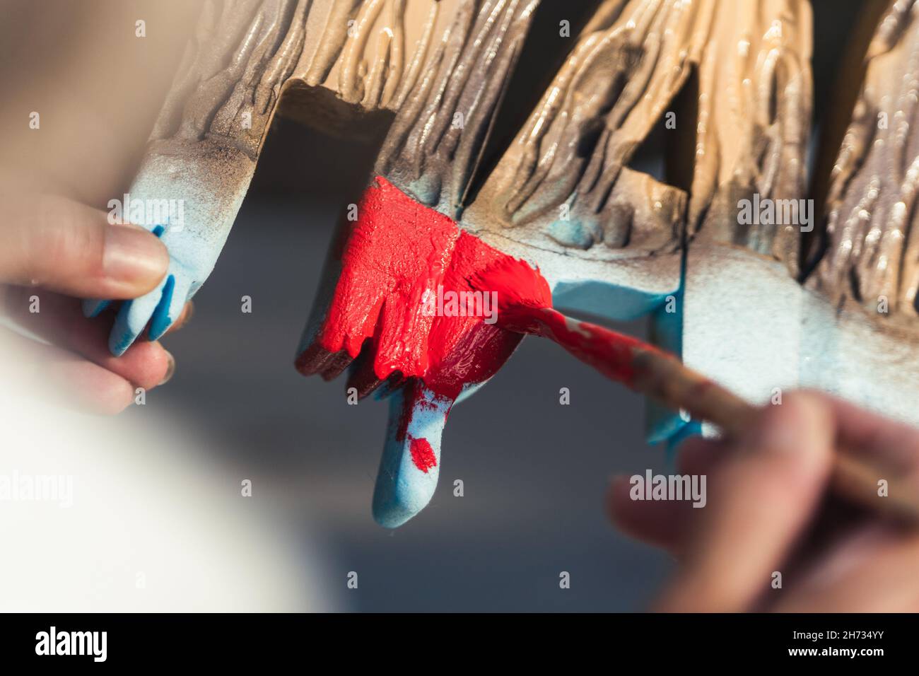 Top view of the hand of a person painting polystyrene letters in red ...