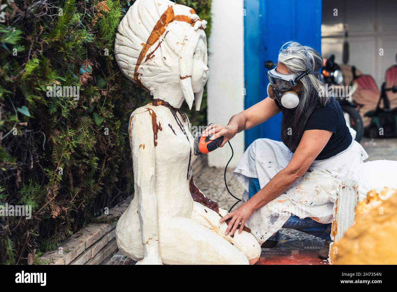Woman with a mask filing a polystyrene sculpture with an electric ...