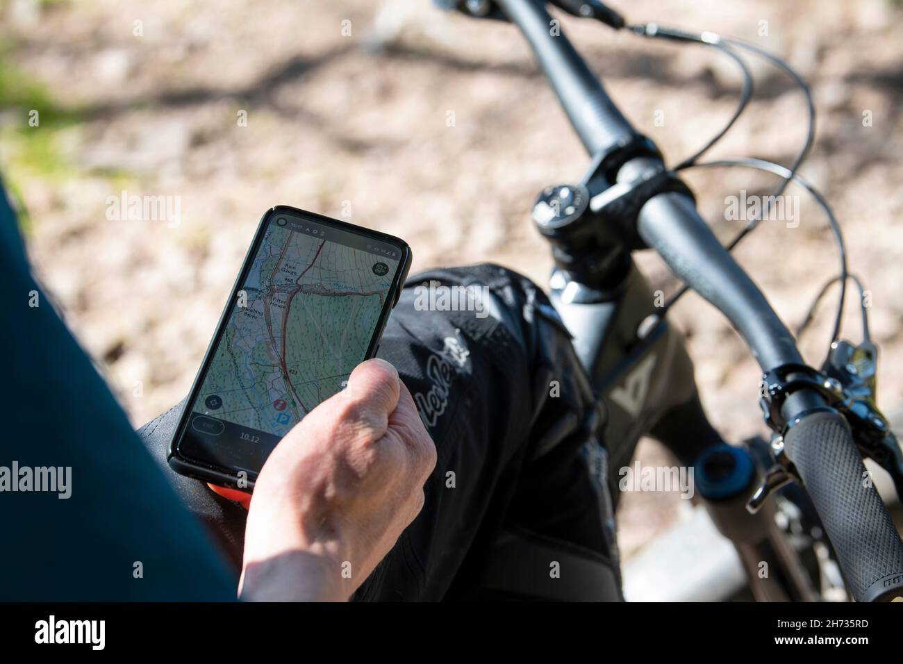 A cyclist riding a mountain bike checks a map on a smart phone in the ...