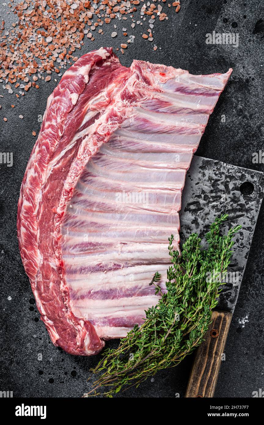 Raw rack of lamb ribs on butcher cutting board with herbs. Black ...
