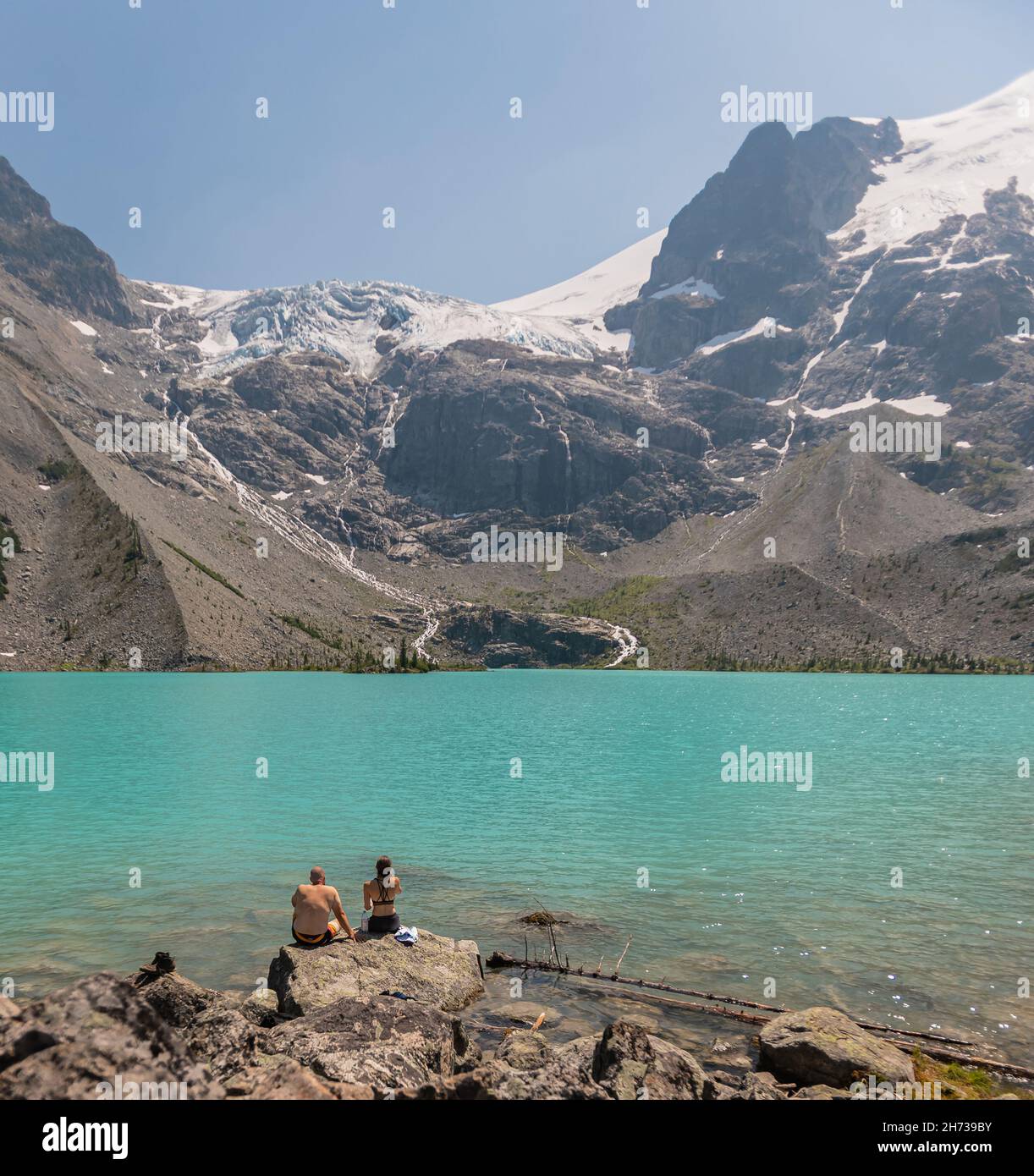 A young couple sits on a big rock and enjoy the majestic view of a ...