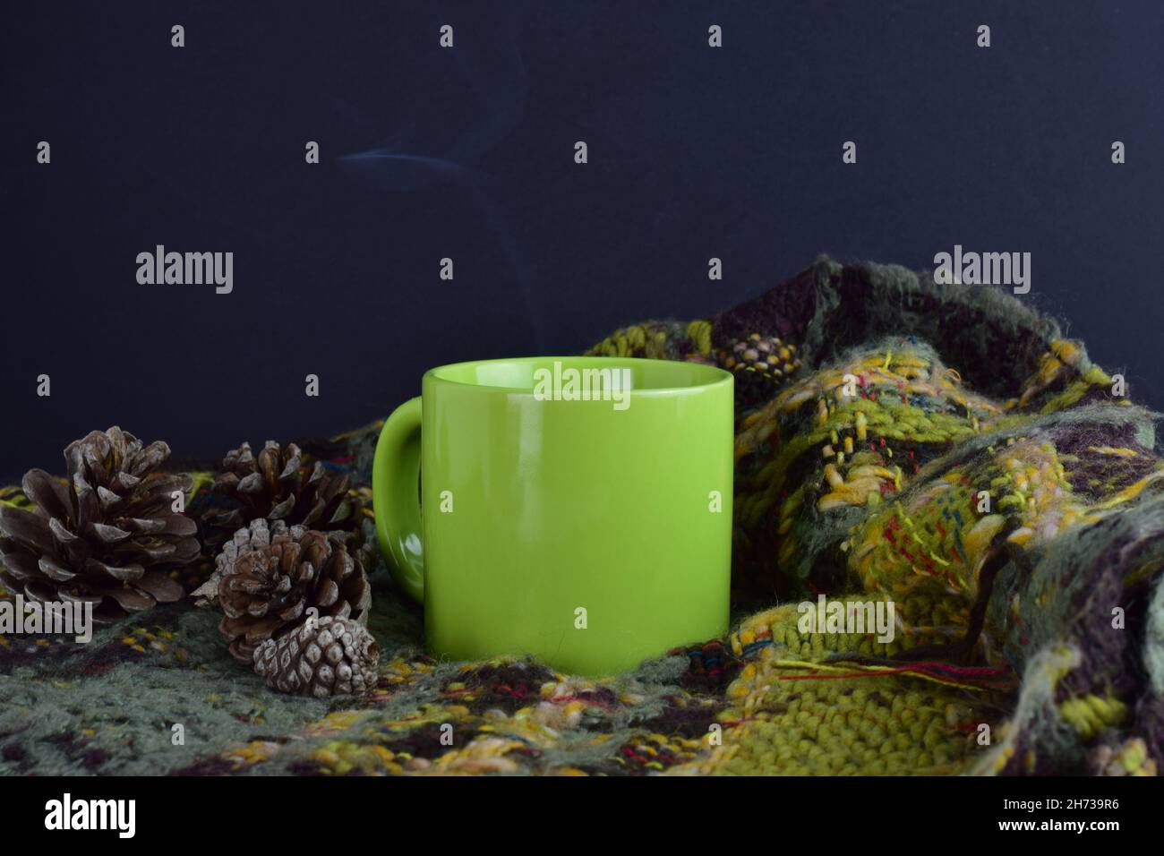 Composition with a green mug, pine cones, and a warm blanket in the ...