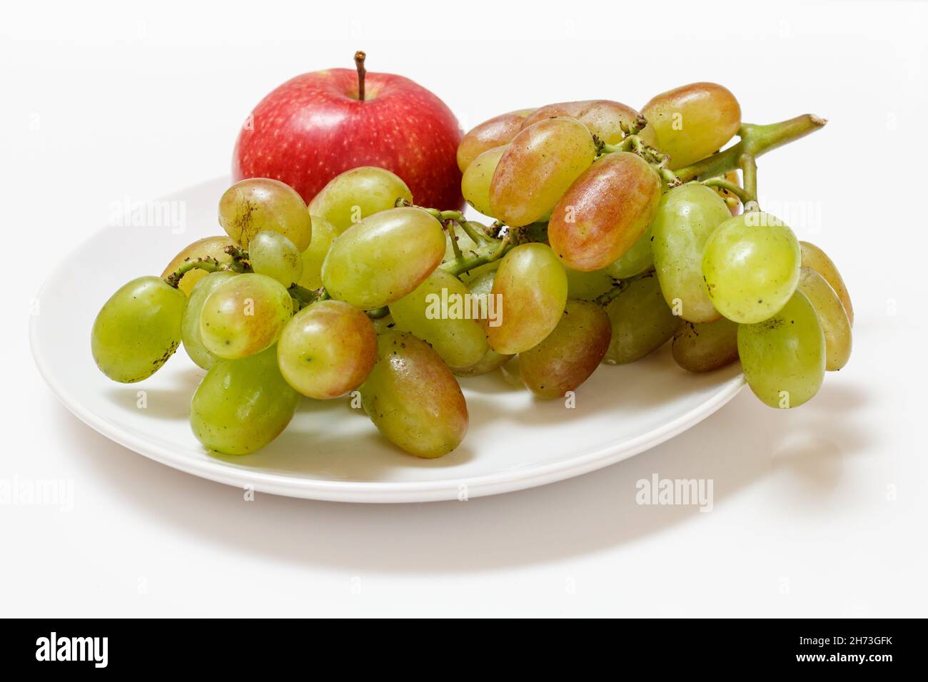 Bunch of green grapes and an apple on a plate with the white background ...