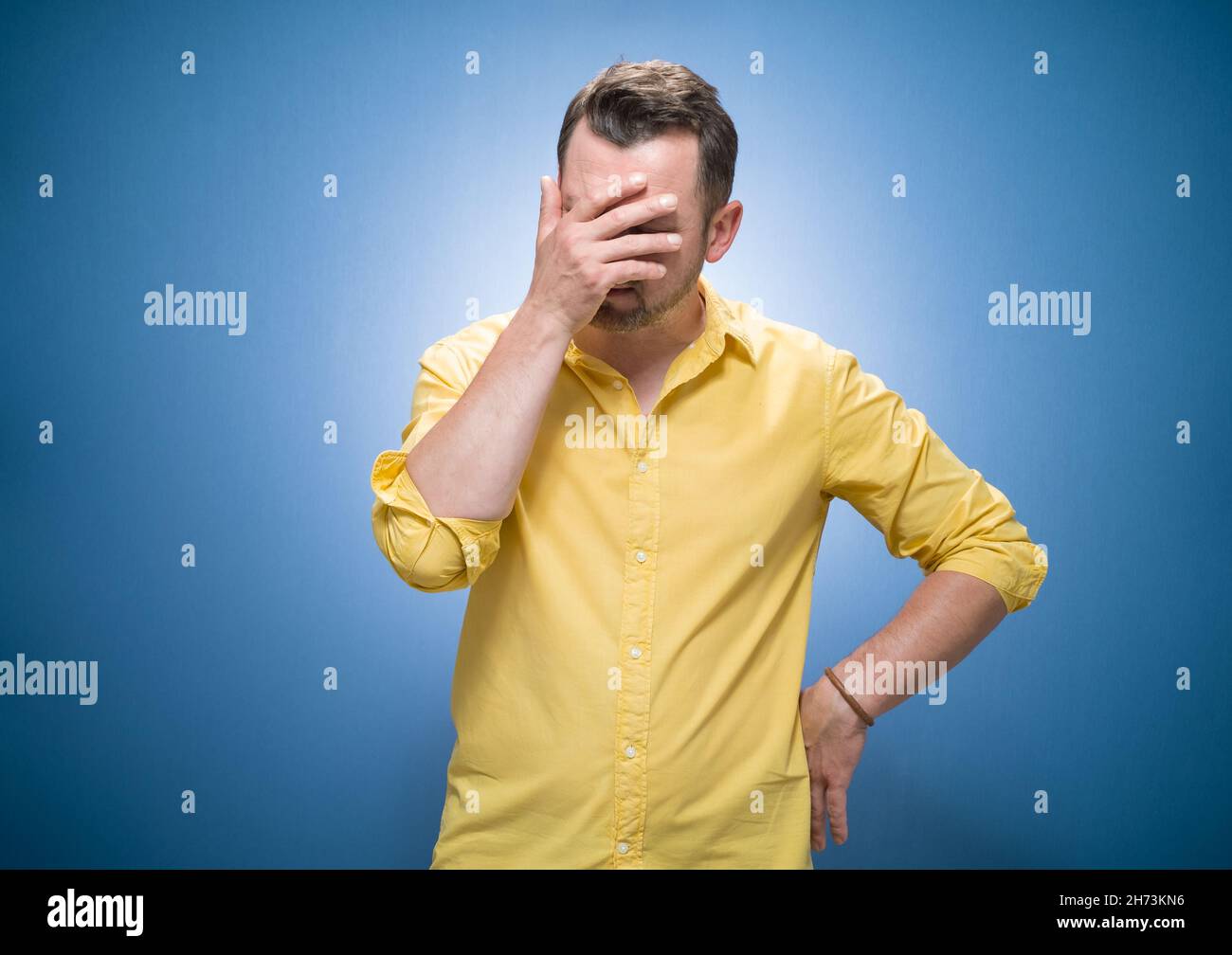 Young man covering face with hand. Shame over blue background, dresses ...
