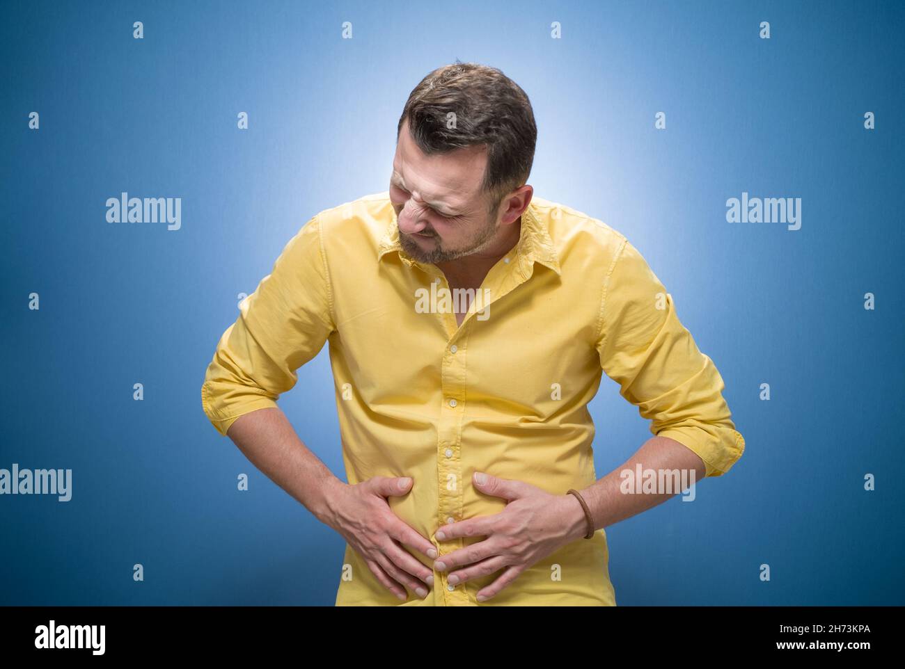 Young man suffering from stomachache - stomach ache over blue ...
