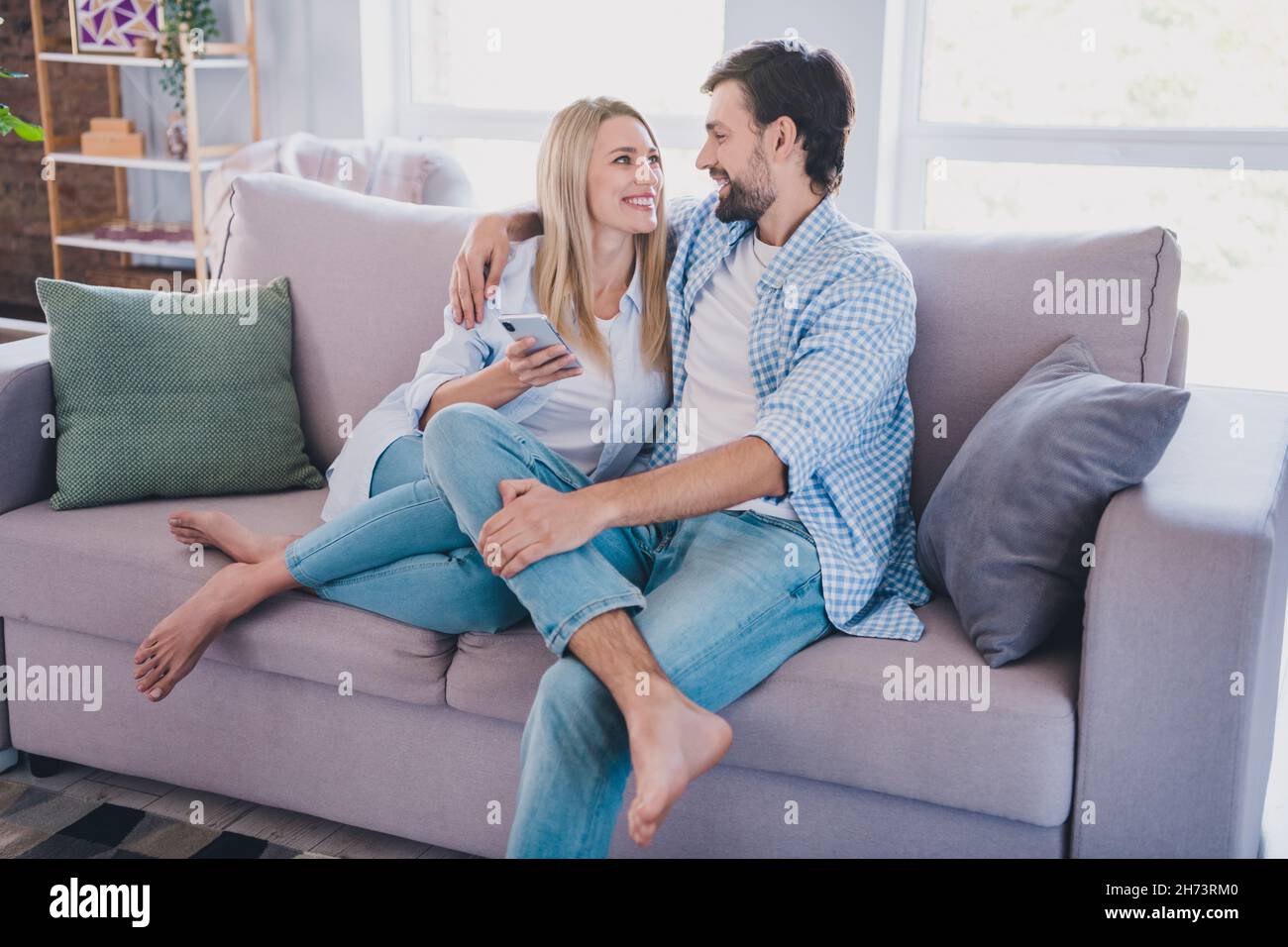 Photo of cheerful couple use mobile social network repost sitting divan flat cuddle romance ...