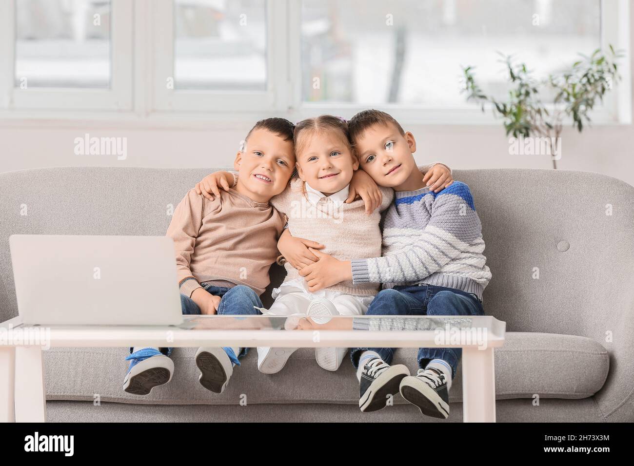 Little children sitting on sofa and watching cartoons on laptop ...