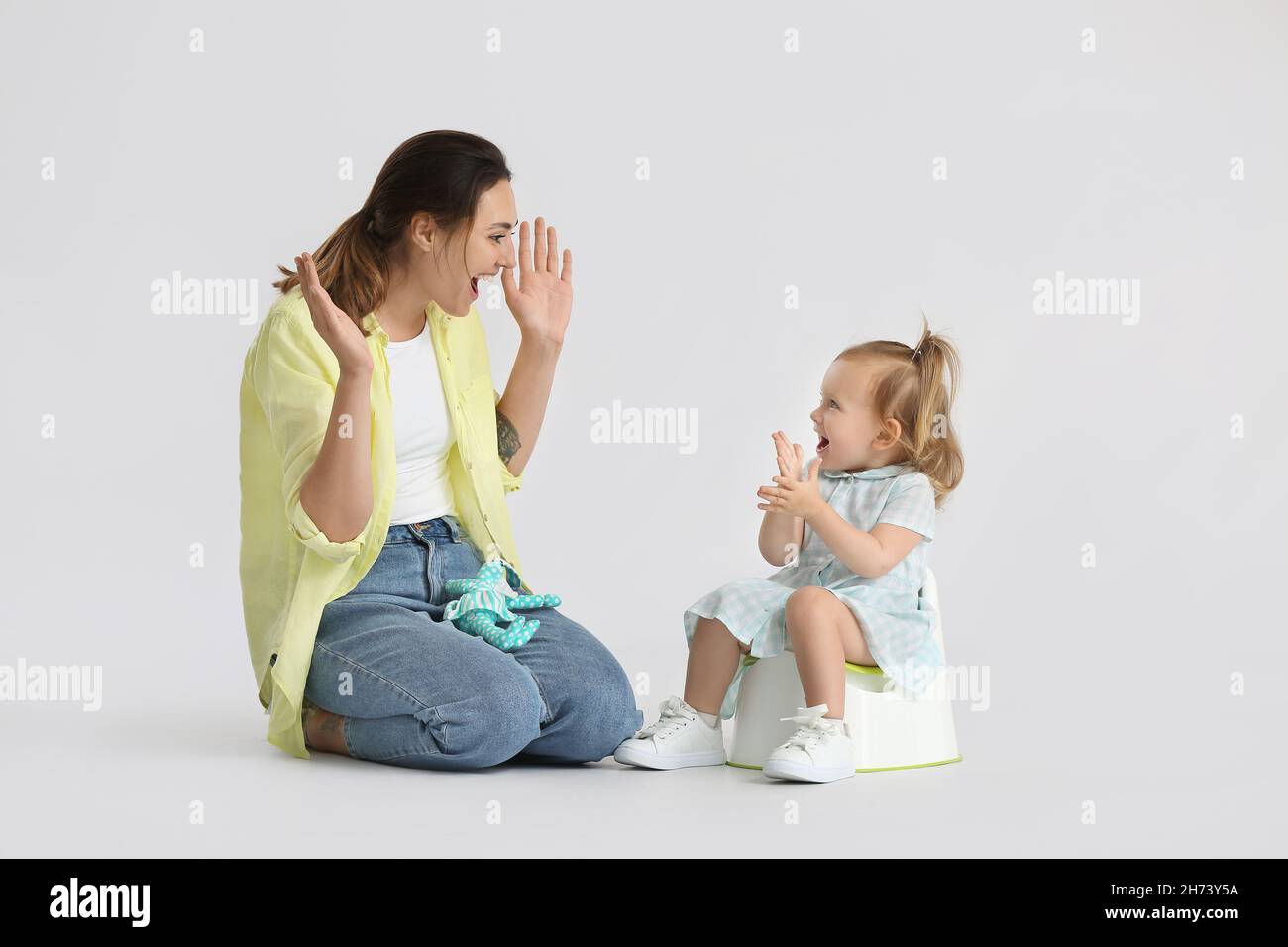 Mother potty training her little daughter on light background Stock ...