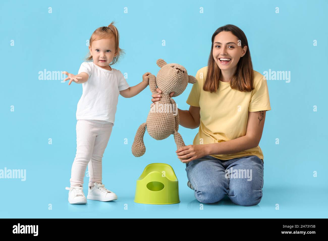 Mother potty training her little daughter on color background Stock ...