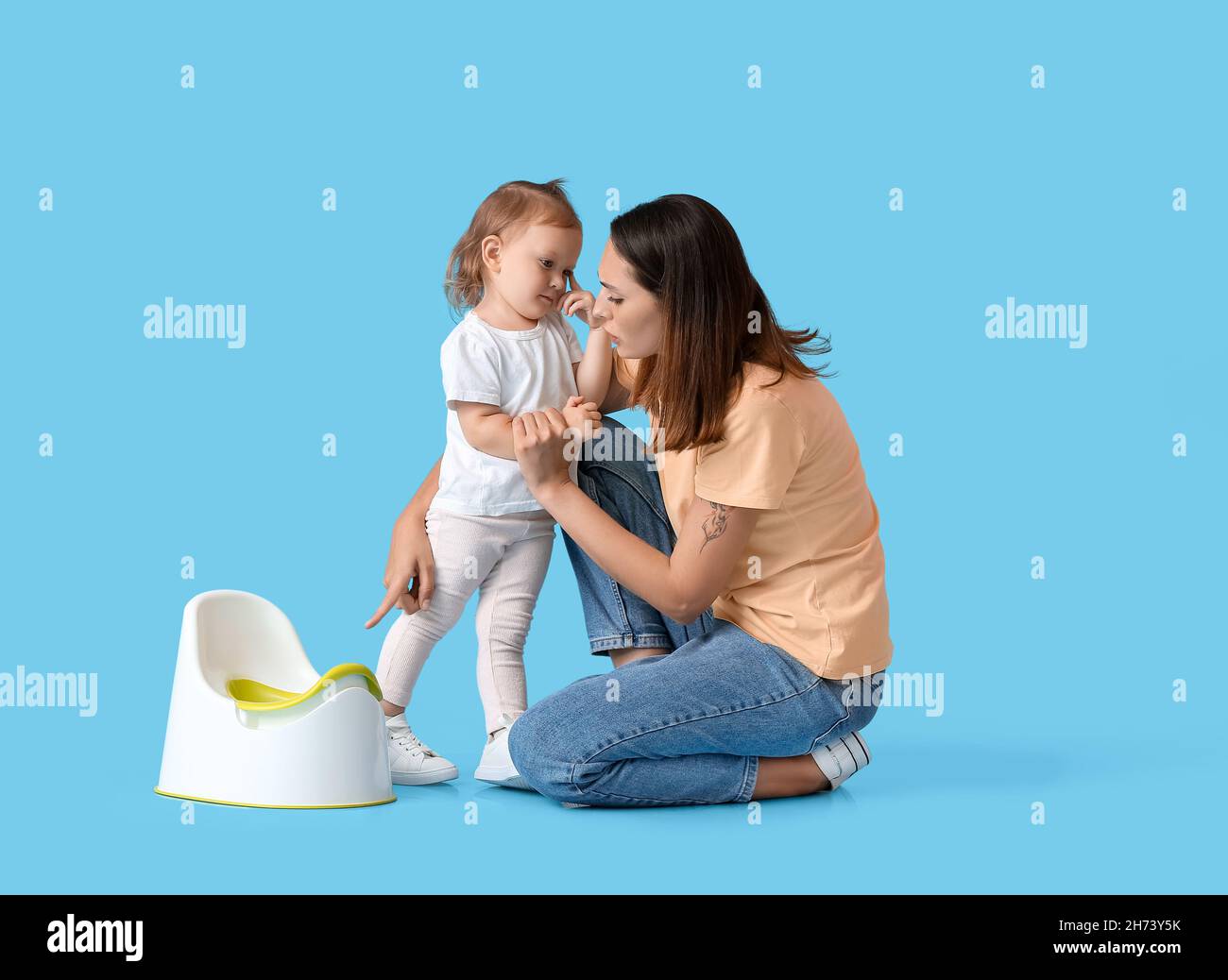 Mother potty training her little daughter on color background Stock ...