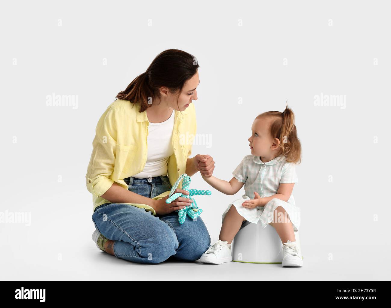 Mother potty training her little daughter on light background Stock ...