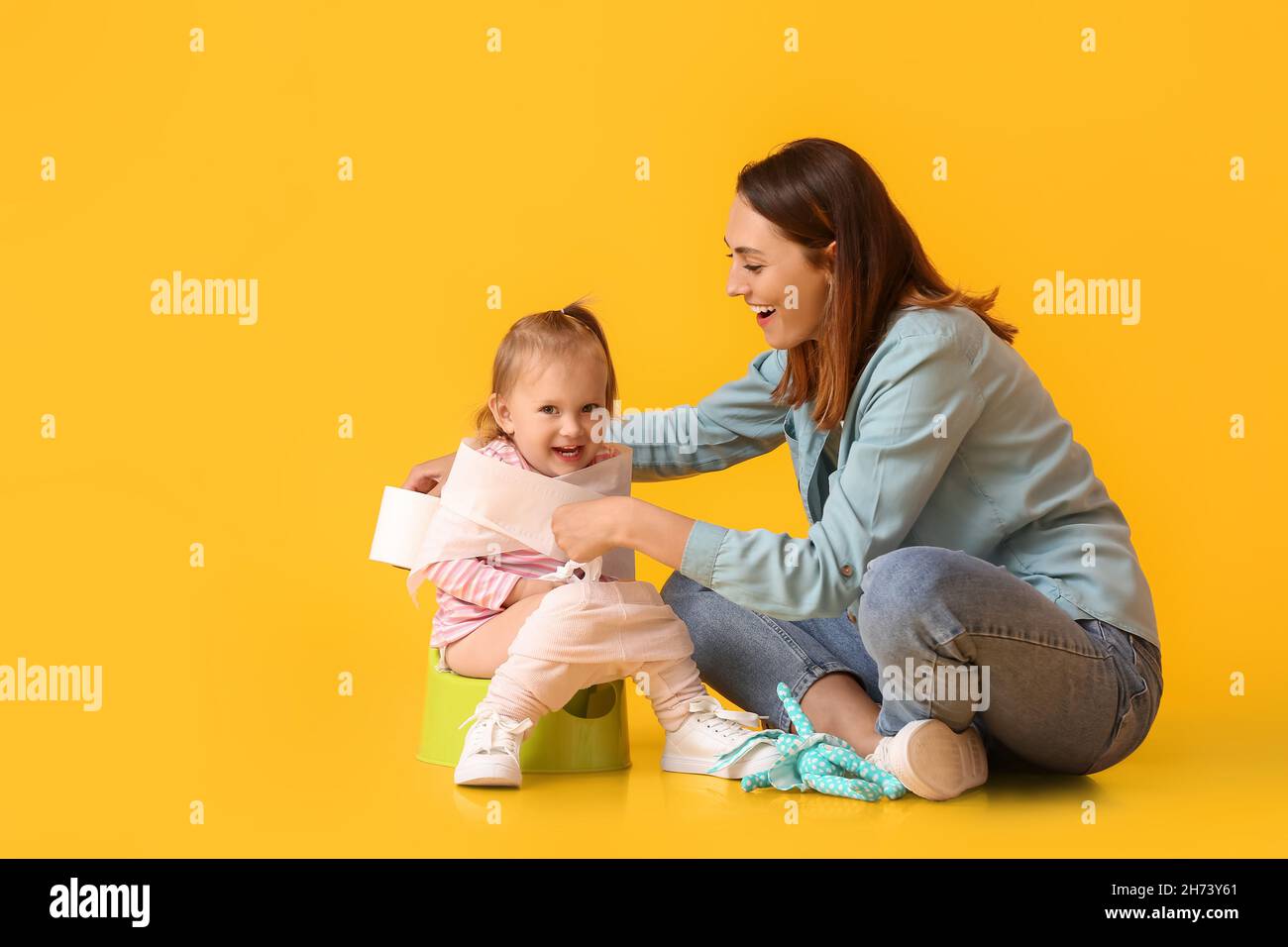 Mother potty training her little daughter on color background Stock ...