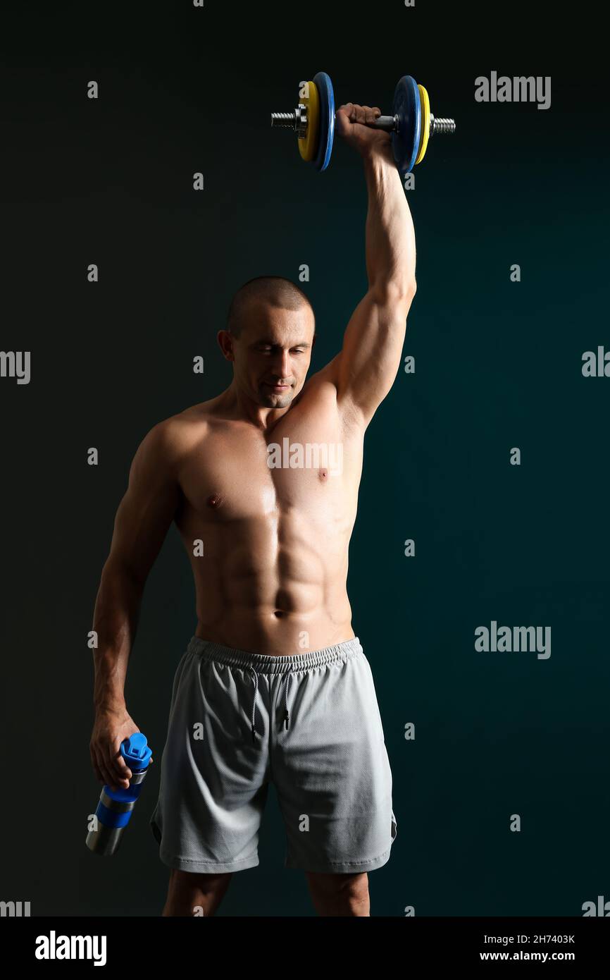 Male bodybuilder with protein shake and dumbbell on dark background ...