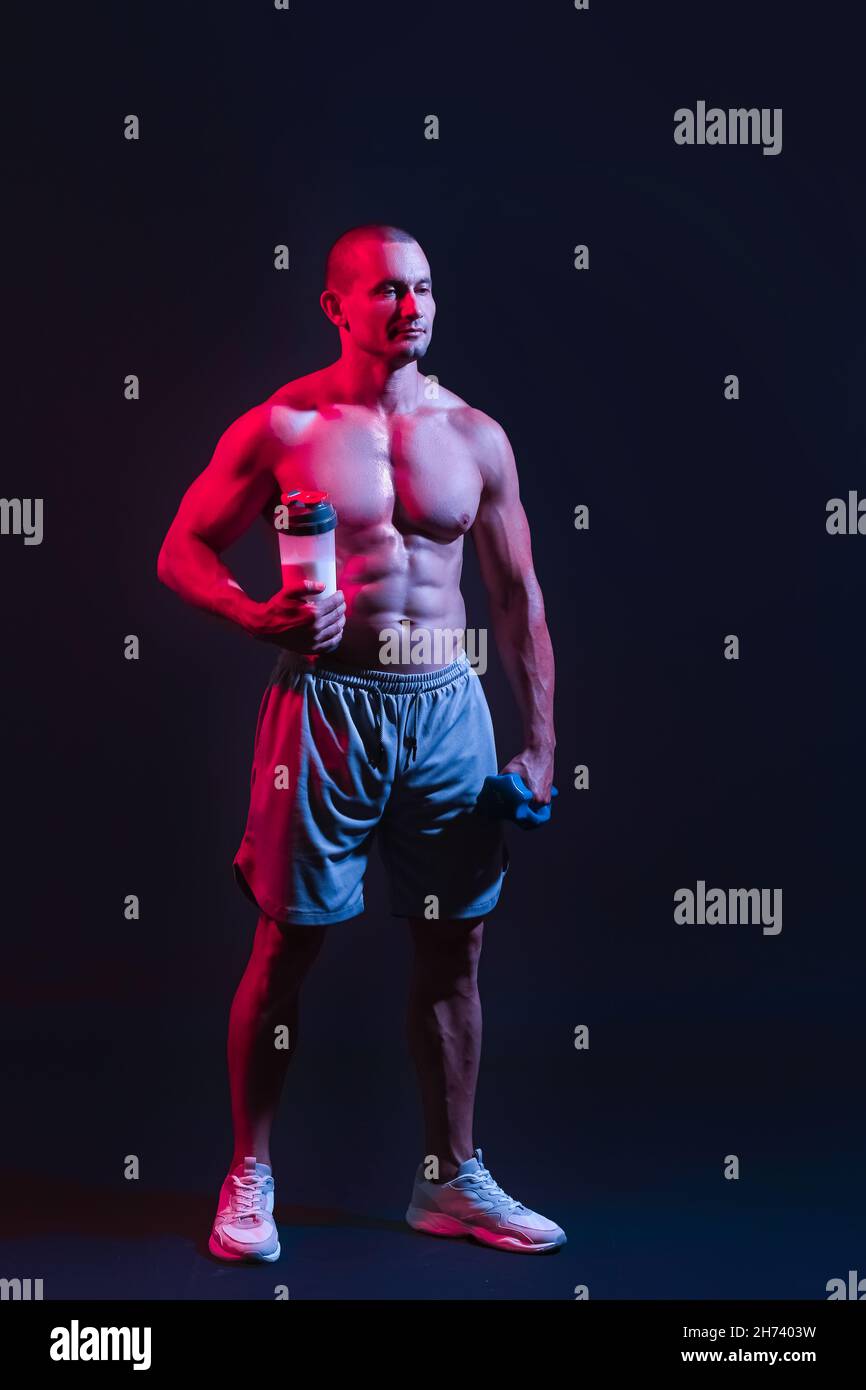 Male bodybuilder with protein shake and dumbbell on dark background ...