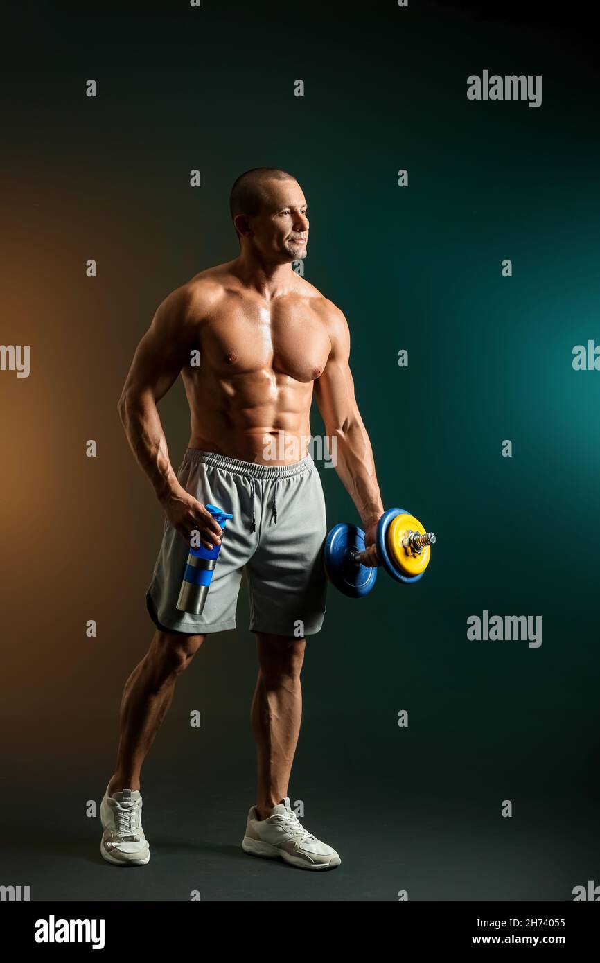 Male bodybuilder with protein shake and dumbbell on dark background ...