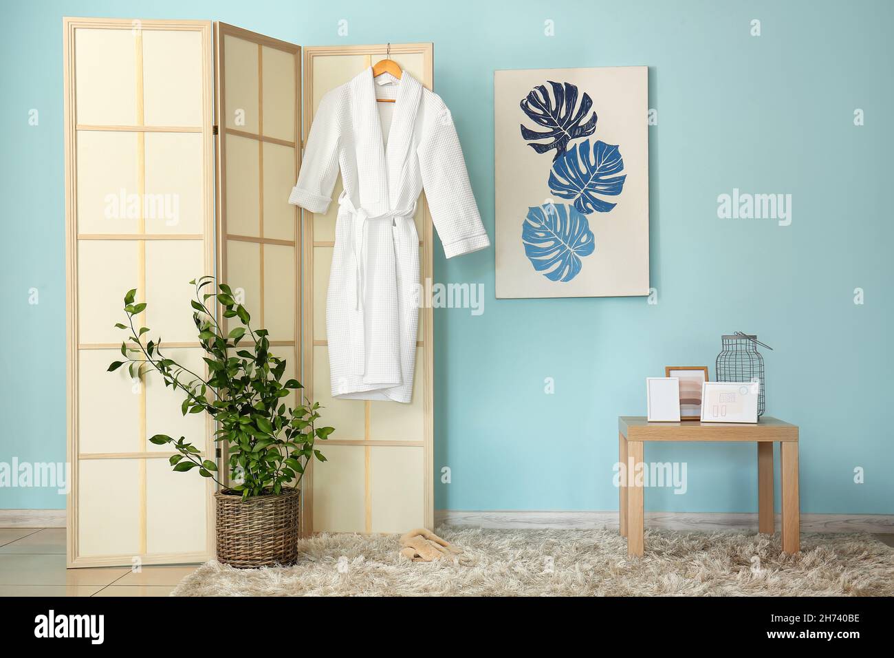 Folding screen with bathrobe, table and frames near blue wall Stock ...