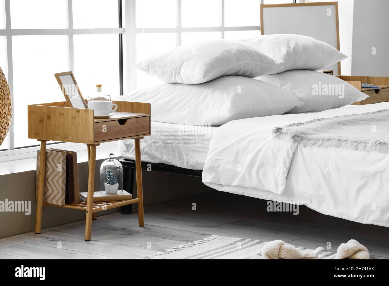 Wooden bedside table and bed near window in room Stock Photo - Alamy