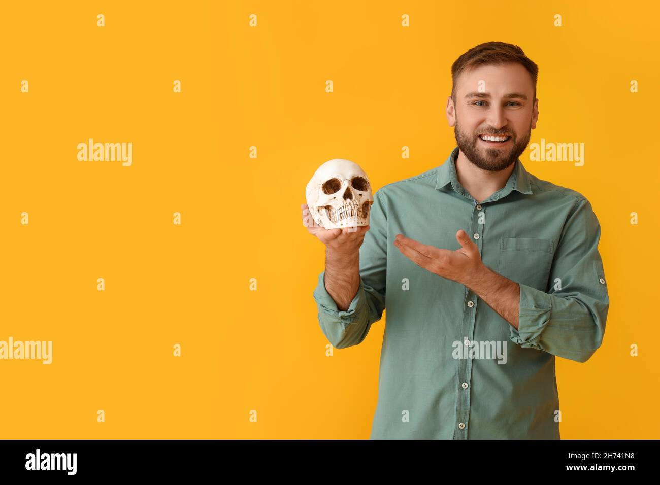 Handsome man with human skull on yellow background Stock Photo - Alamy